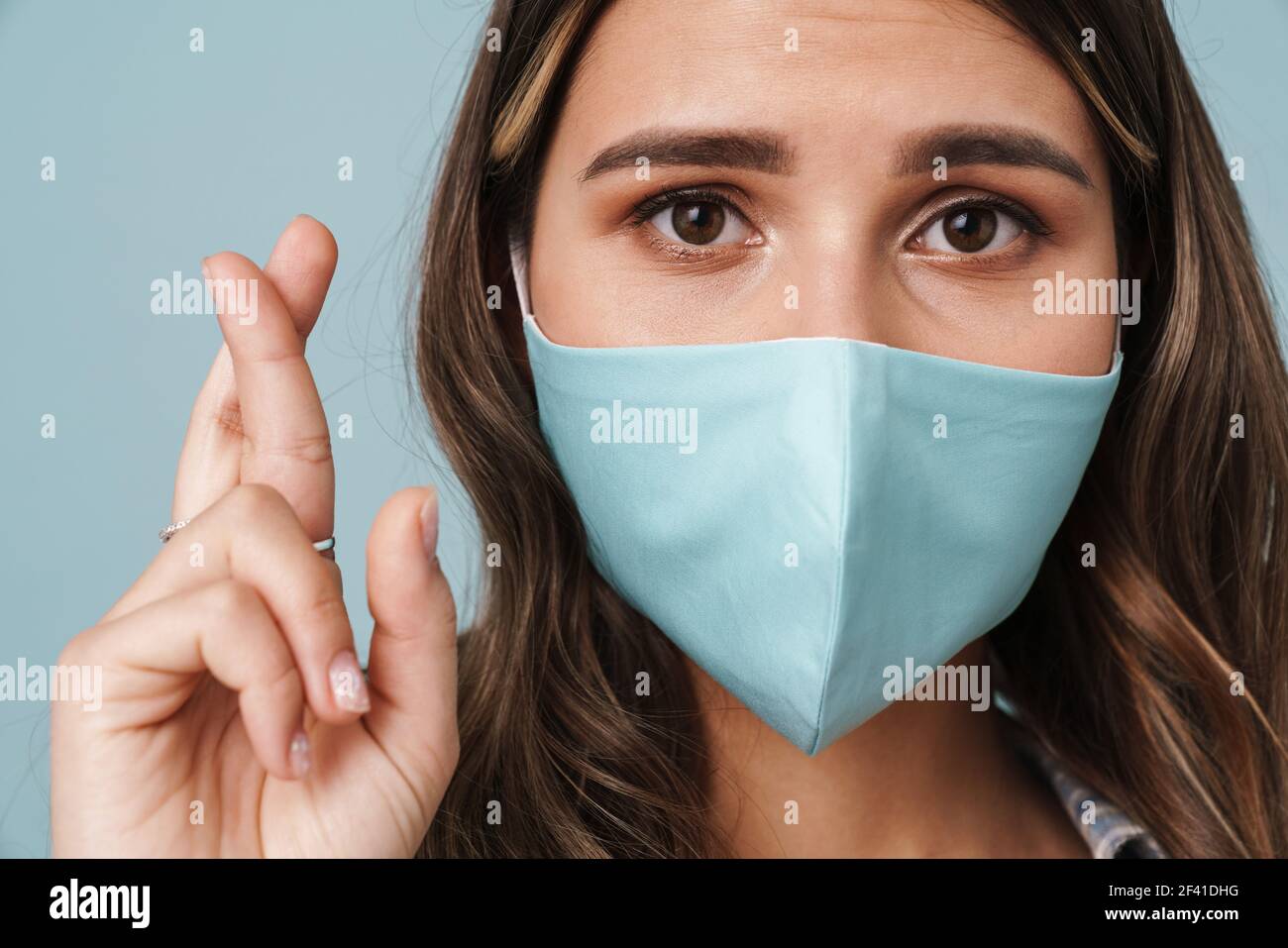 Charming girl in face mask posing with fingers crossed for good luck ...