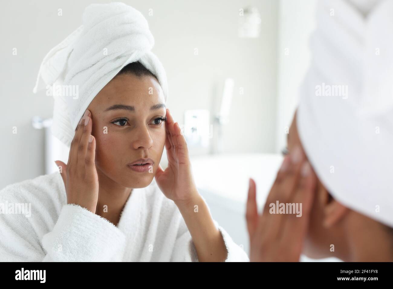 African American Woman In Bathrobe Touching Her Face While Looking In