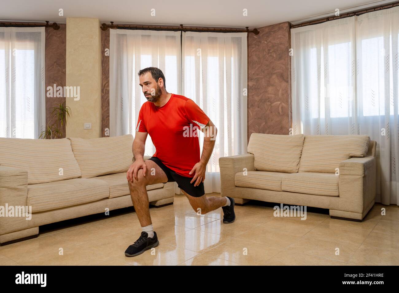 Fit bearded man in black and red sportswear doing stretching exercise ...