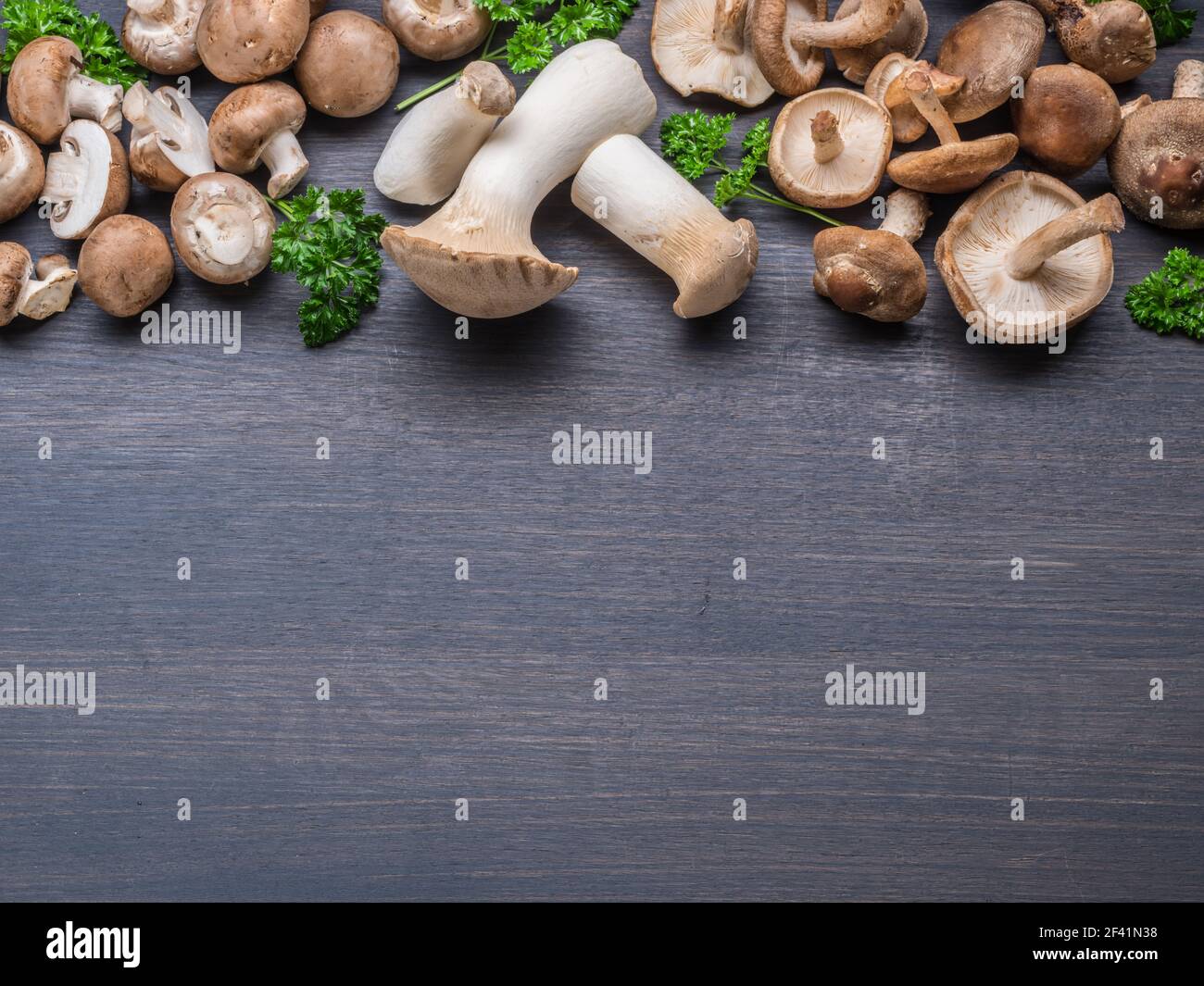 Different brown colored edible mushrooms on black table with herbs. Top ...