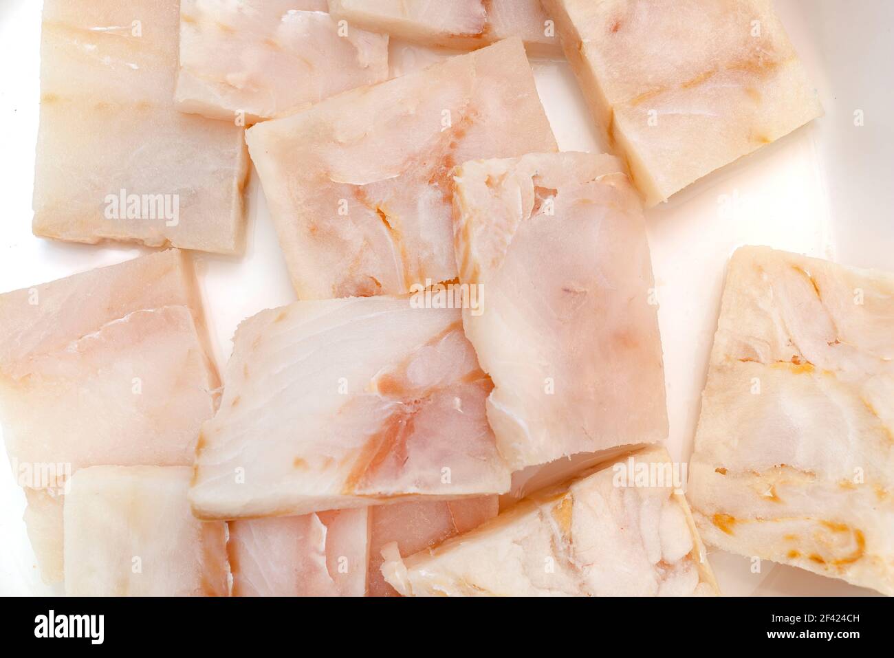 A fresh cod fish fillet cut into squares lying on a white plate, top ...