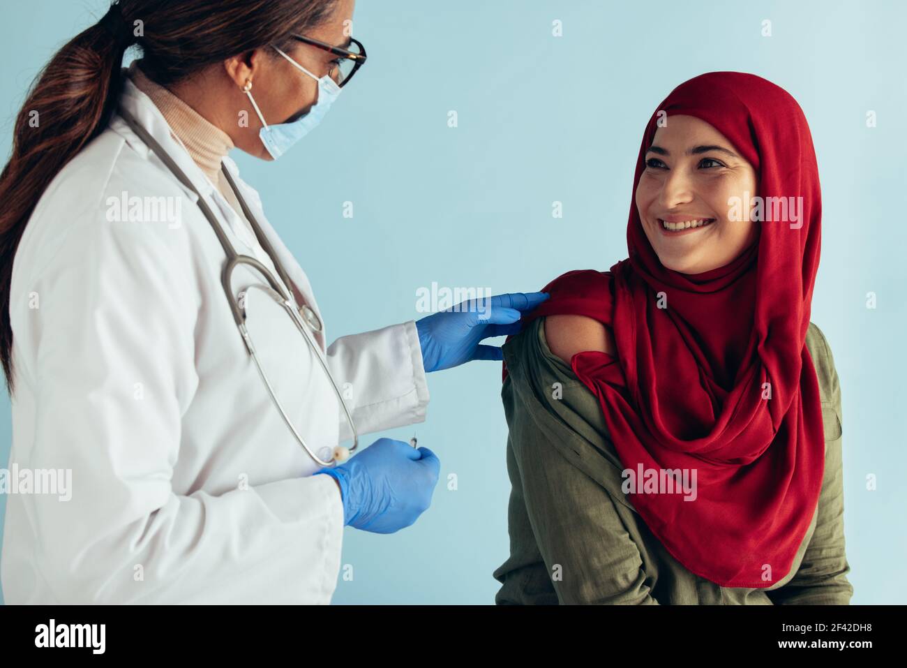 Smiling Islamic woman in hijab getting vaccine from a female doctor ...