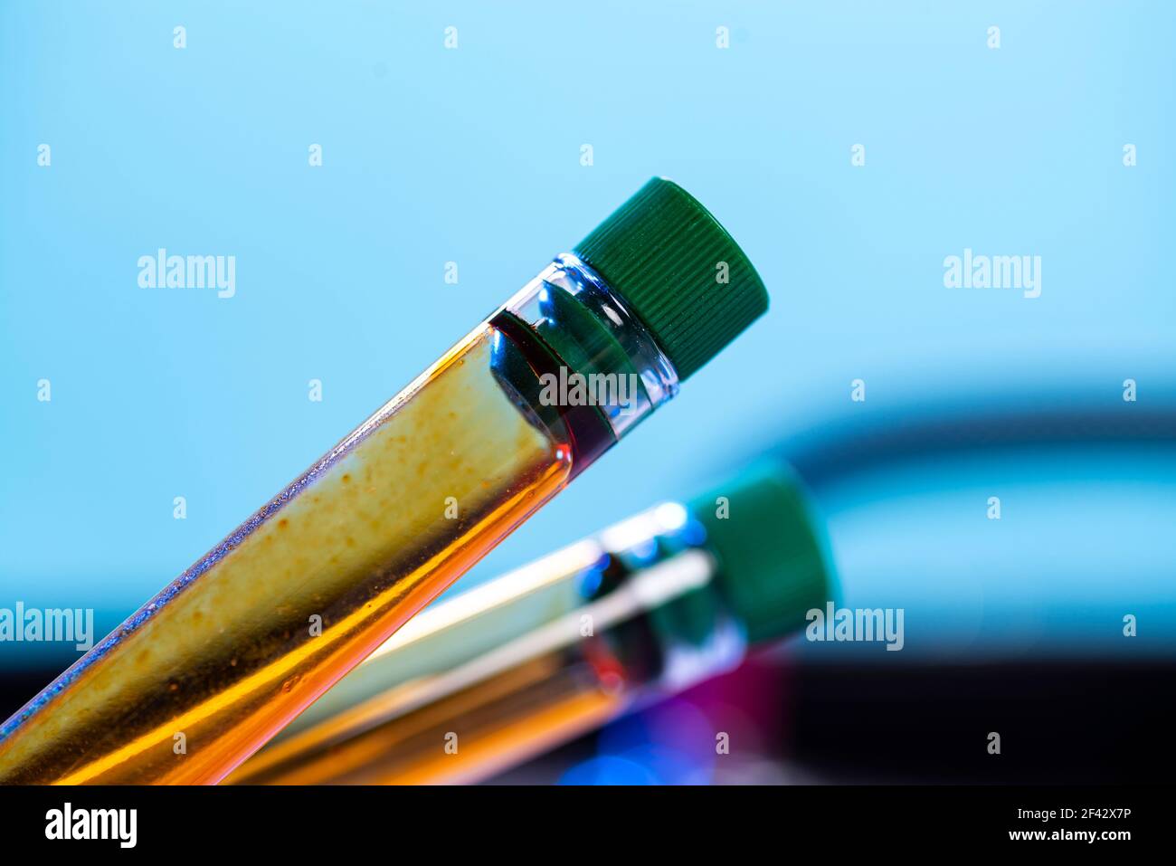 Two chemical test tubes with closed lids with orange liquid on blue ...