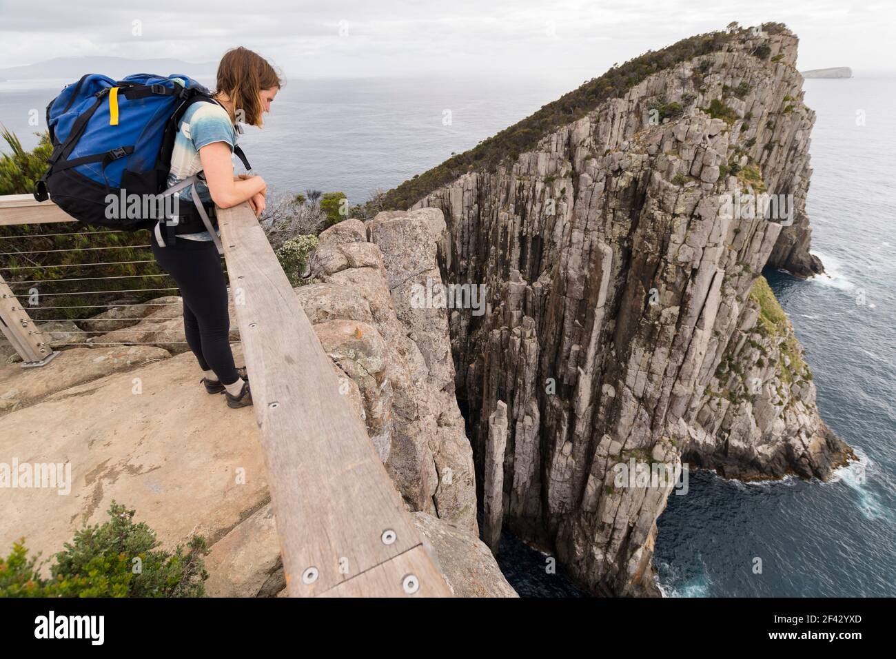 Woman leans over handrail on top of sea cliff in Tasman National Park ...