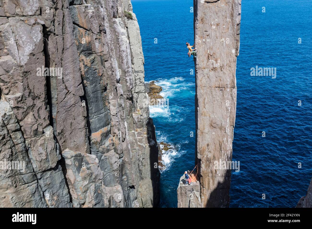 Athletic woman rockclimbs an exposed rock column with her partner ...