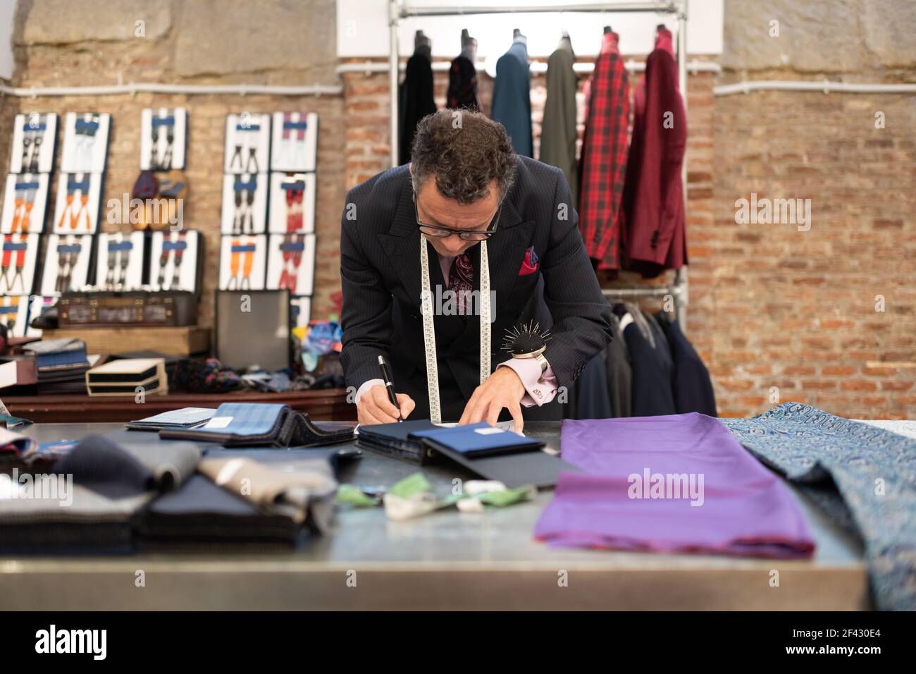 Mature tailor drawing sketches near clothes Stock Photo - Alamy