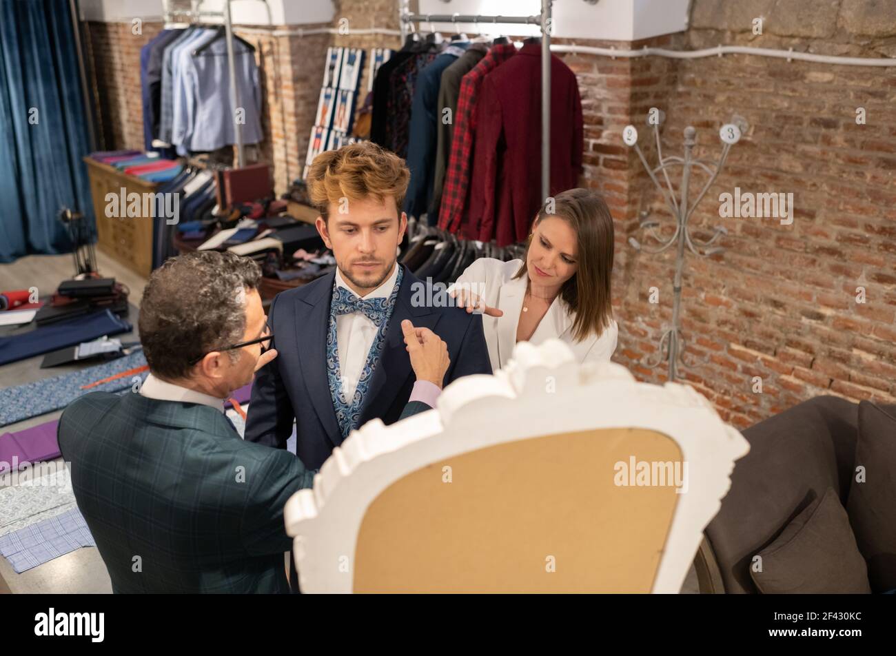 Tailor and assistant fitting suit on client Stock Photo - Alamy