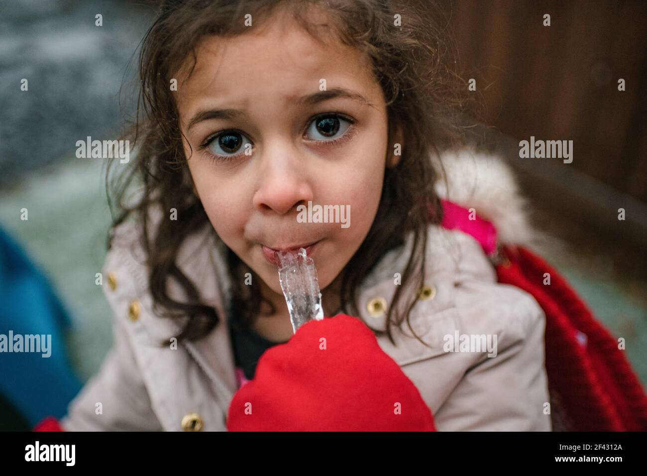 Happy preschool girl eating icicle with mittens Stock Photo - Alamy