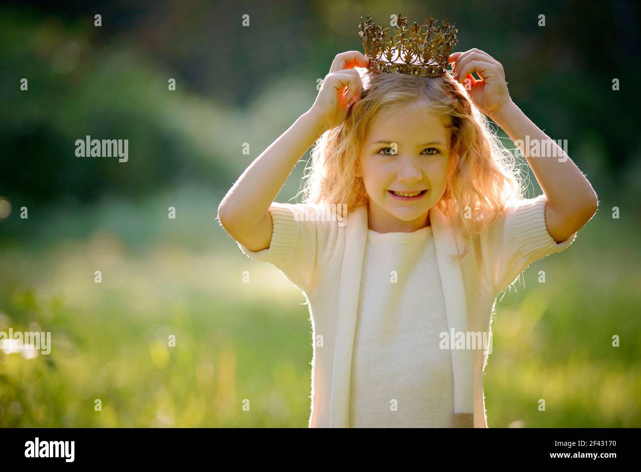 Beautiful little blond girl putting on a crown outdoors Stock Photo - Alamy