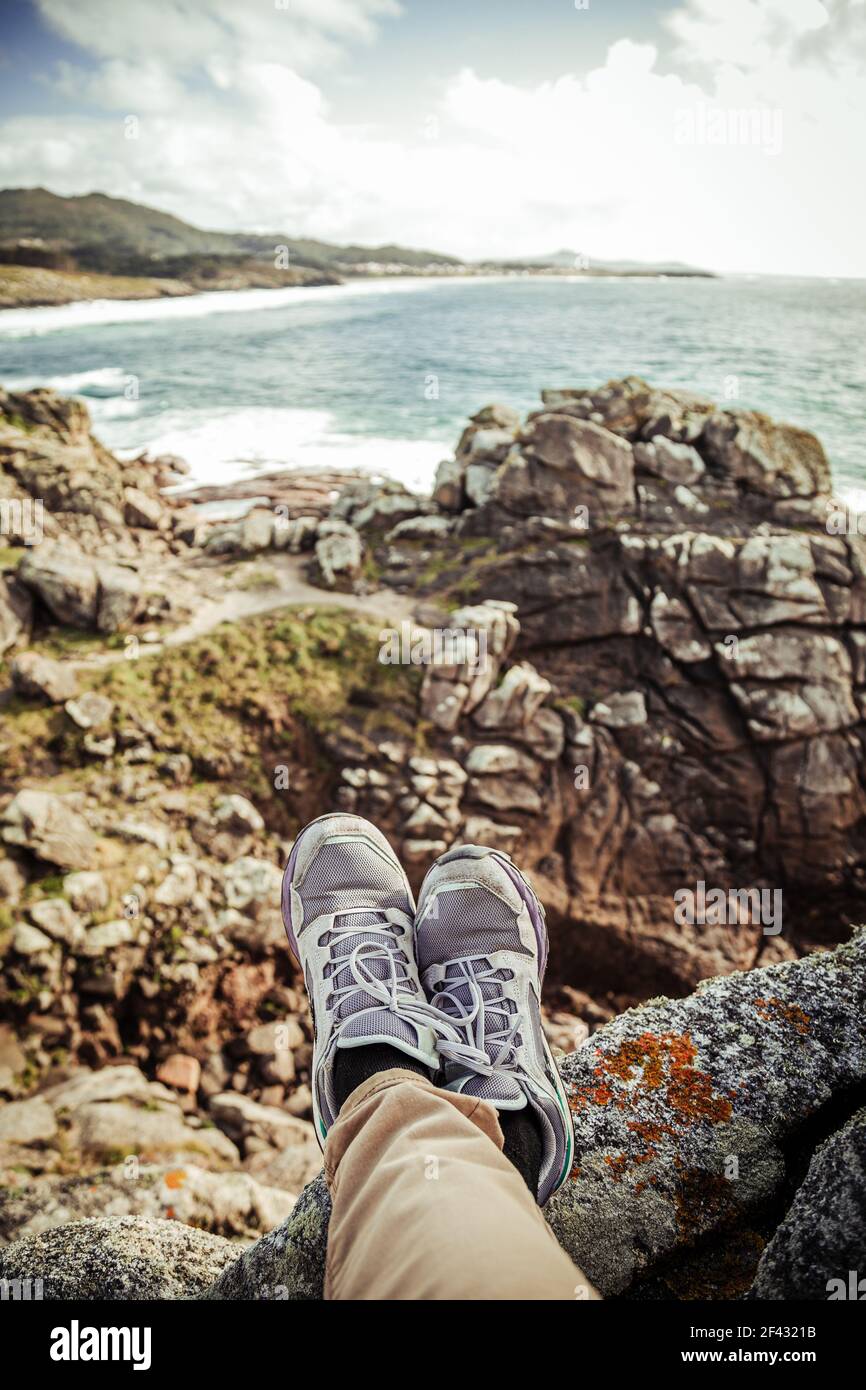 Feet of a man sitting on top of the cliff overlooking the sea Stock ...