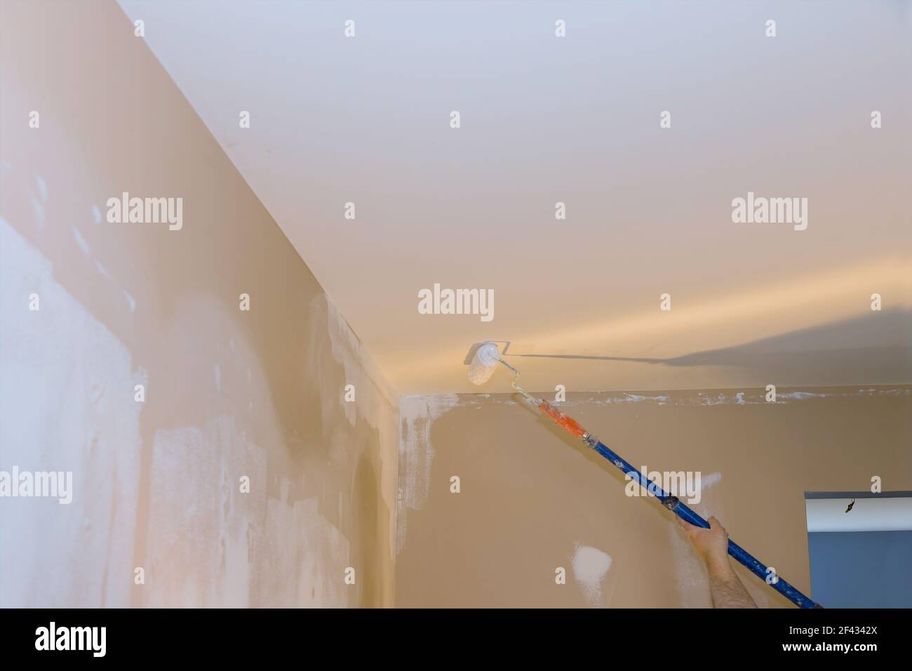 Worker priming with a paint roller with repair the ceiling wall after ...