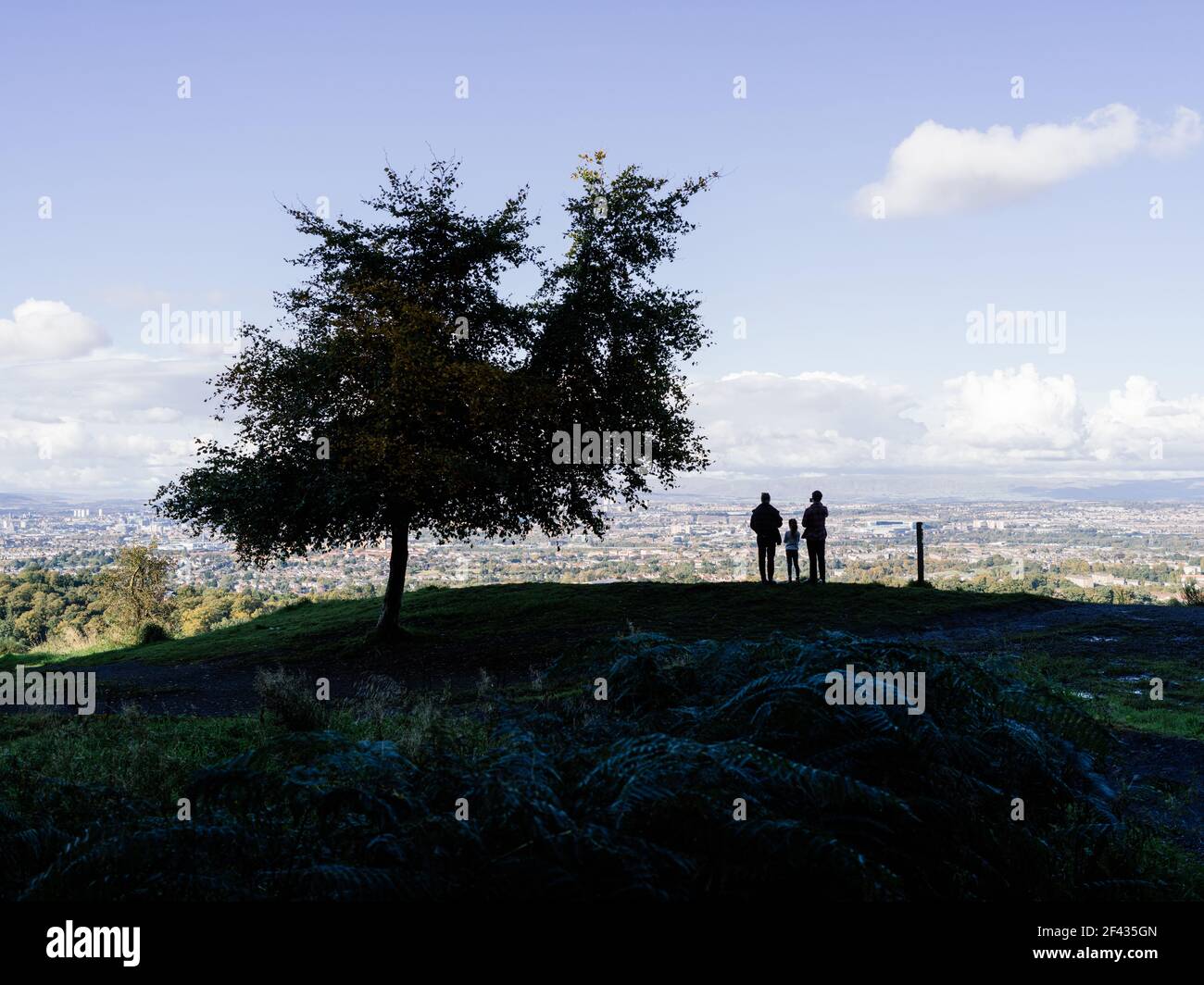 Family of three people standing next to a tree enjoying the view and ...