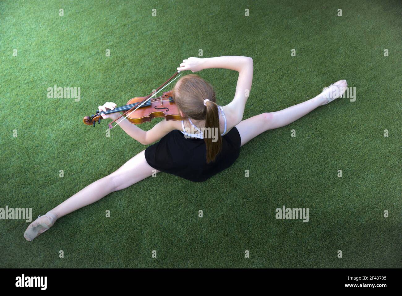 girl in spagat ballet pose playing the violin on green grass placed ...