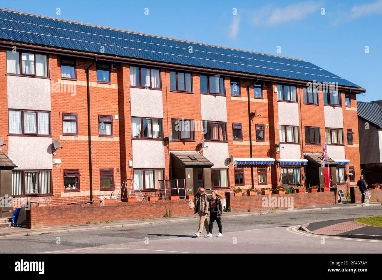 People walking past a large three storey block of flats with the roof ...