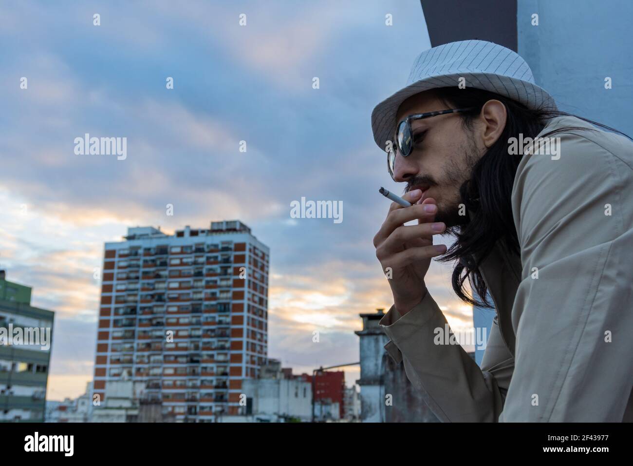 young hipster with long hair smoking cigarette. man with hat and ...