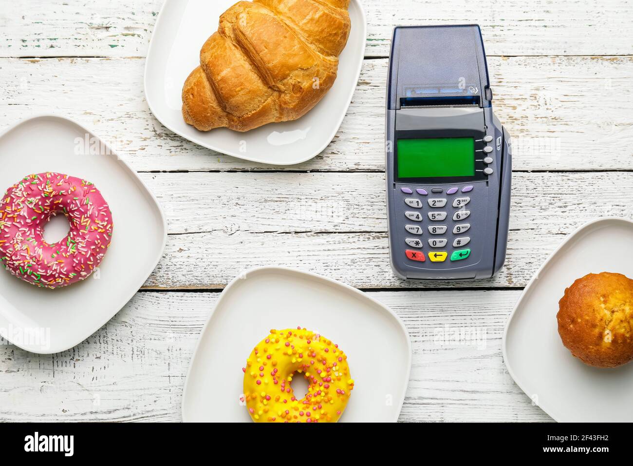 Payment terminal with donuts and croissant in plates on light wooden ...