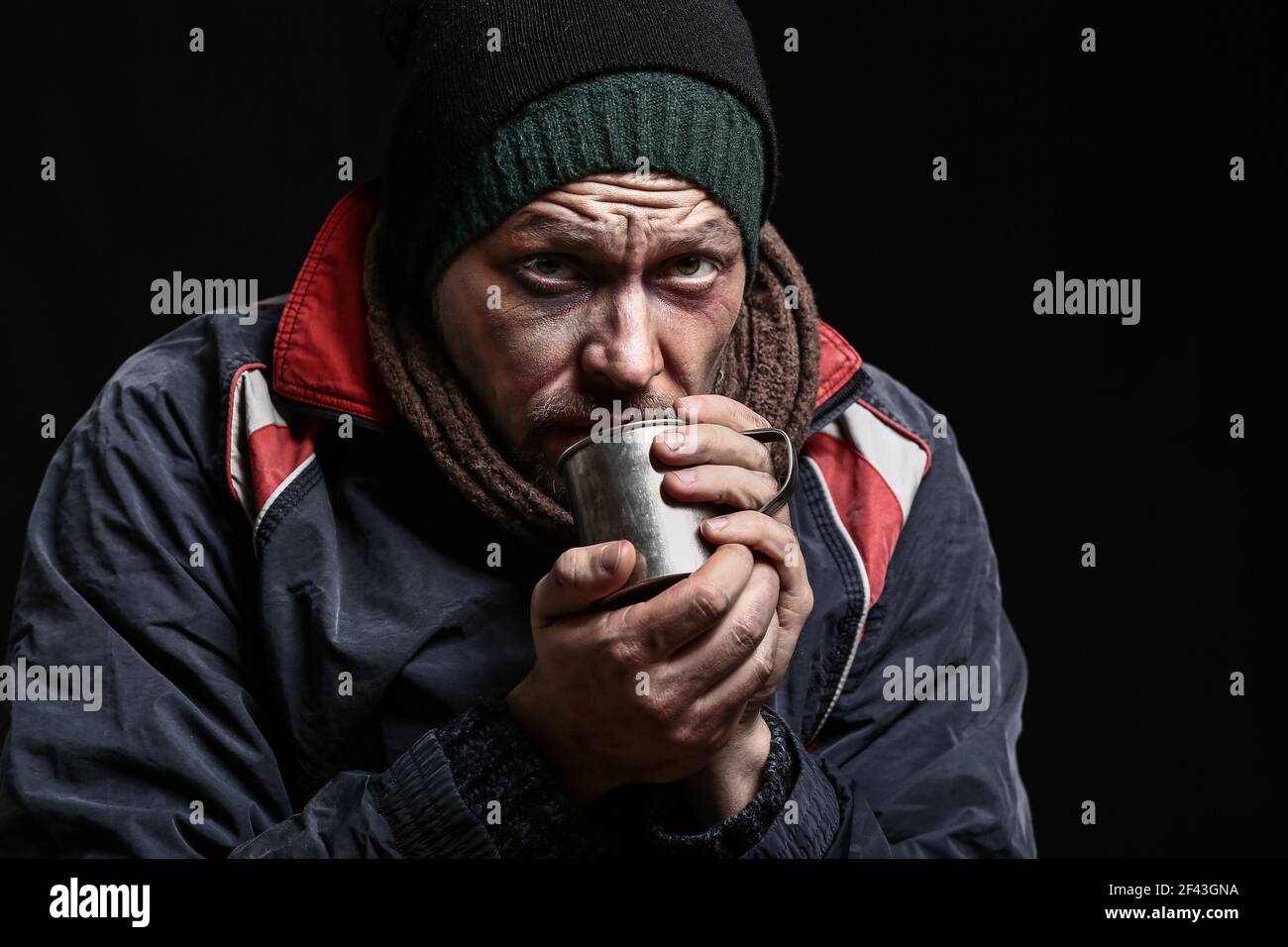 Portrait of poor homeless man with cup of hot drink on dark background ...