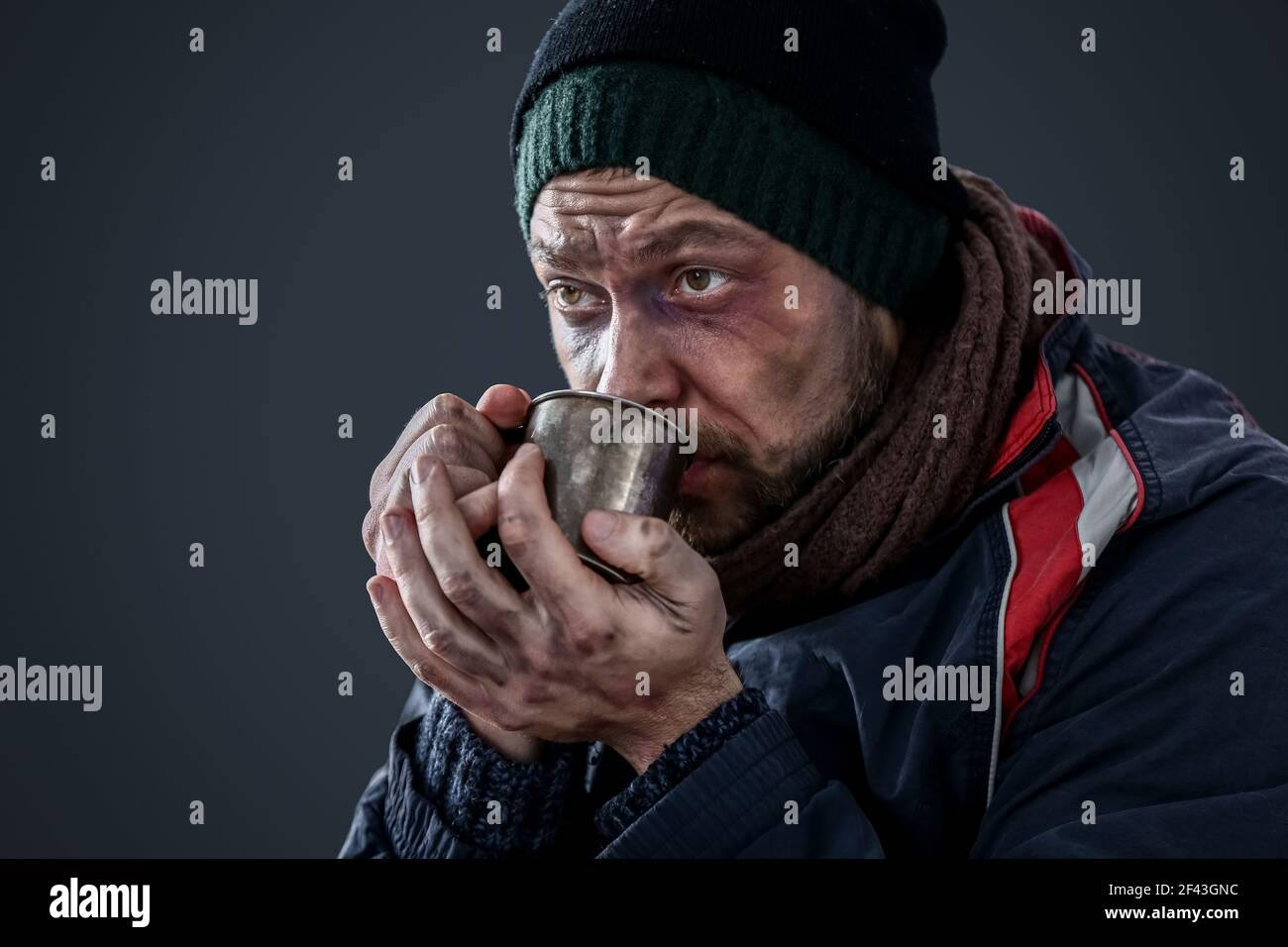 Portrait of poor homeless man with cup of hot drink on dark background ...
