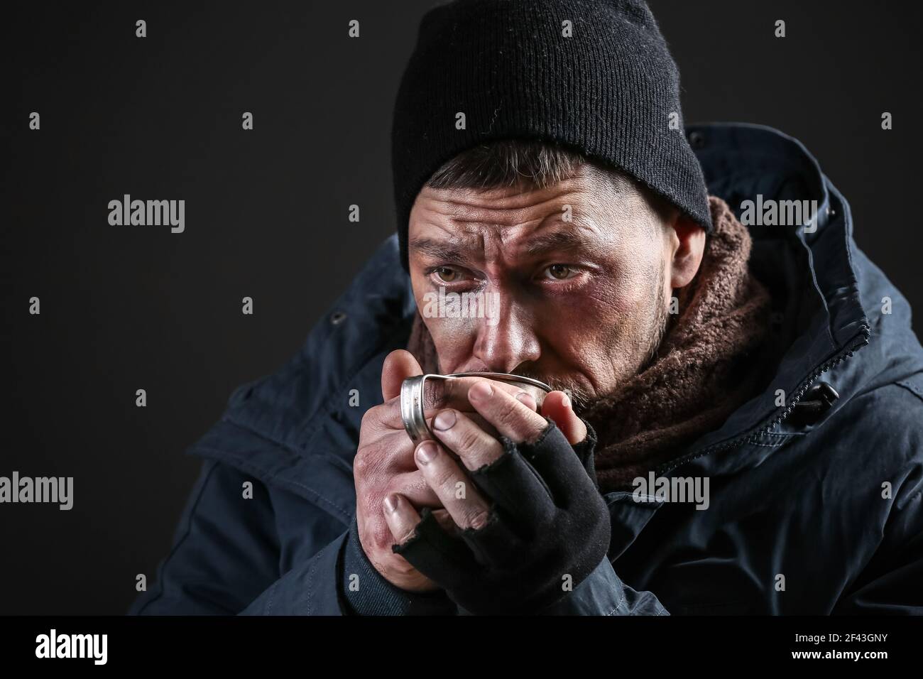Portrait of poor homeless man with cup of hot drink on dark background ...