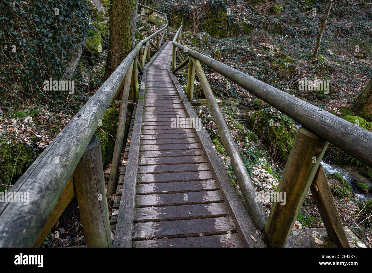 An old wooden bridge with water cascade flowing through big rocks in ...