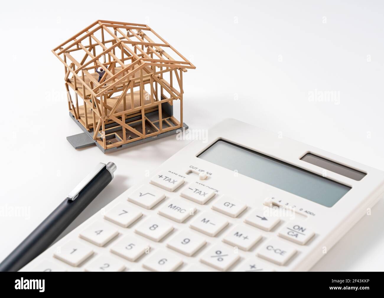 A model of a house, a calculator, and a pen on a white background with ...