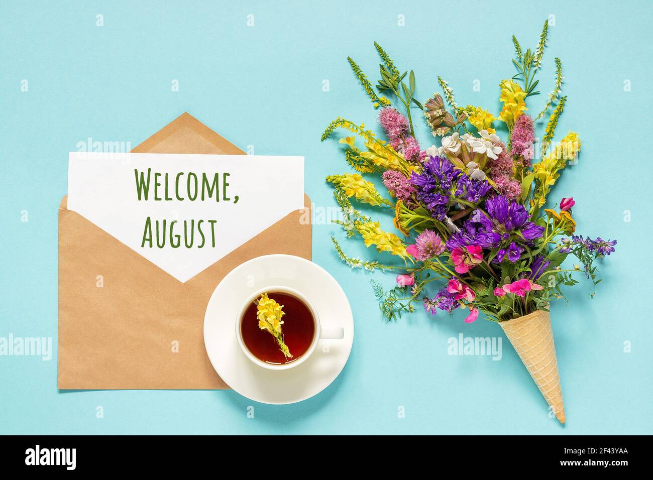 Welcome August text on paper card in craft envelope, cup of tea and ...