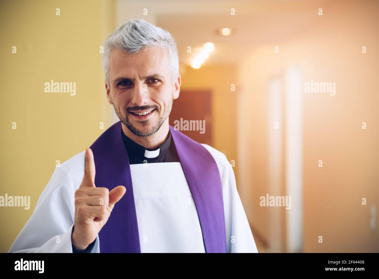 Priest man standing with a smile on face, pointing with hand finger ...