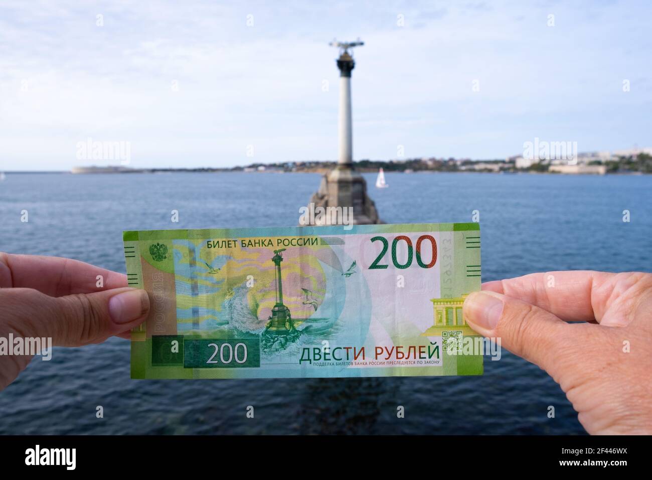 banknote of 200 Russian rubles in women's hands against the background of the monument to sunken ...