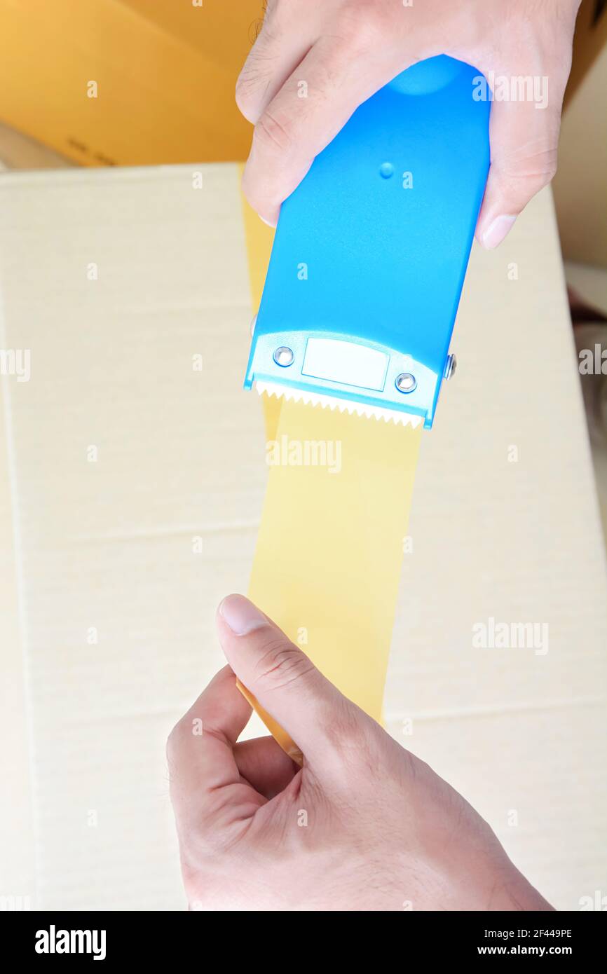 Hands holding masking tape dispenser, taping a box Stock Photo - Alamy