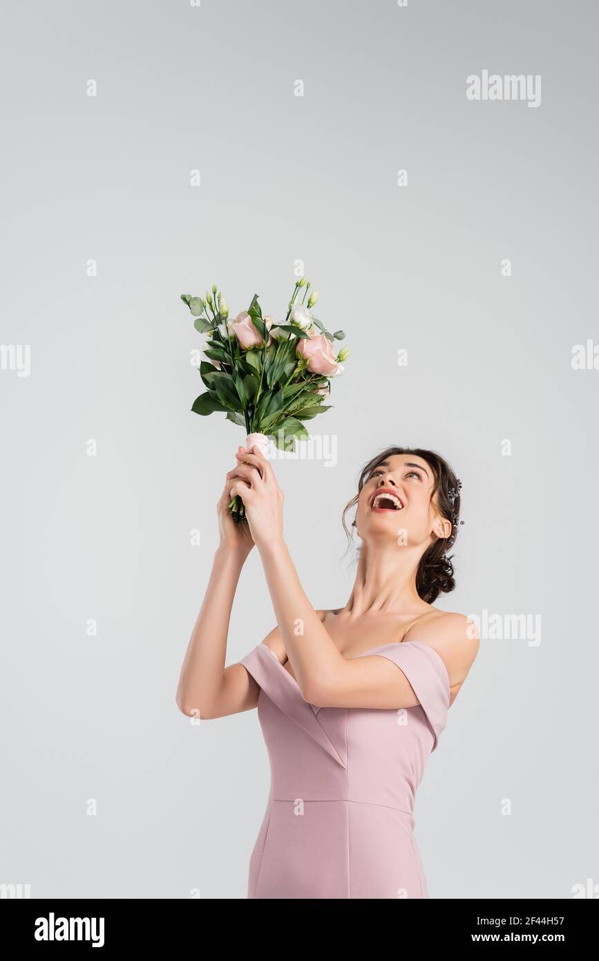 excited bride in pink dress throwing wedding bouquet isolated on grey ...