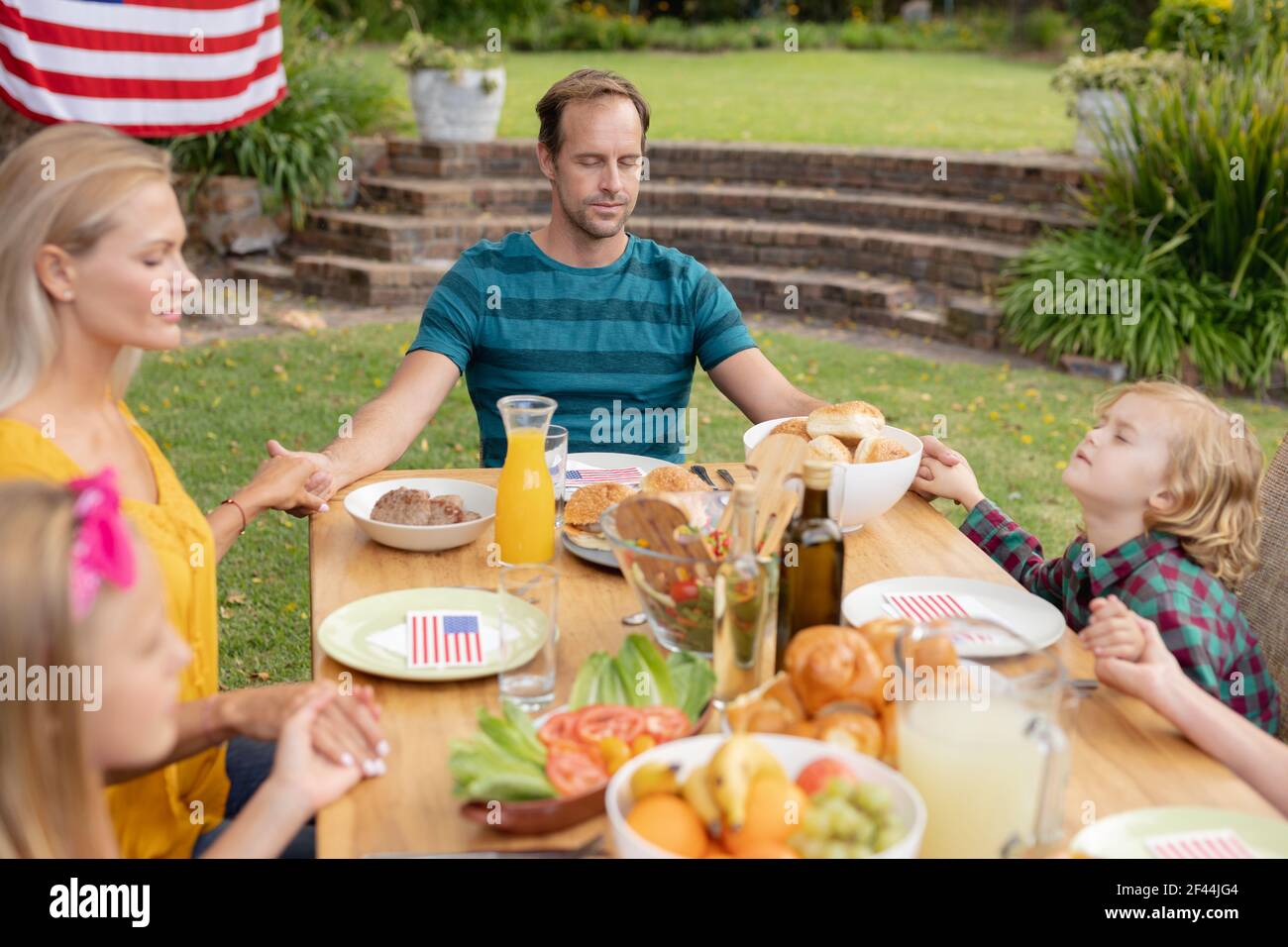 Caucasian man and family holding hands saying grace before eating meal ...
