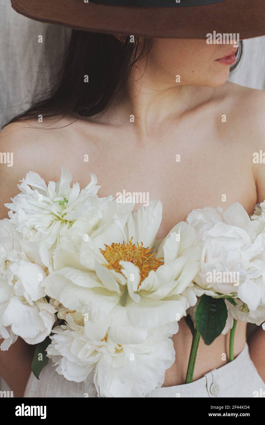 Portrait of stylish sensual woman in hat with white peony flowers on body. Beautiful young ...
