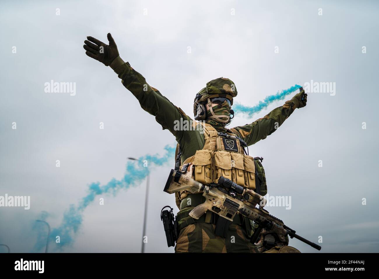 A shallow focus of an armed special force soldier holding a blue smoke ...