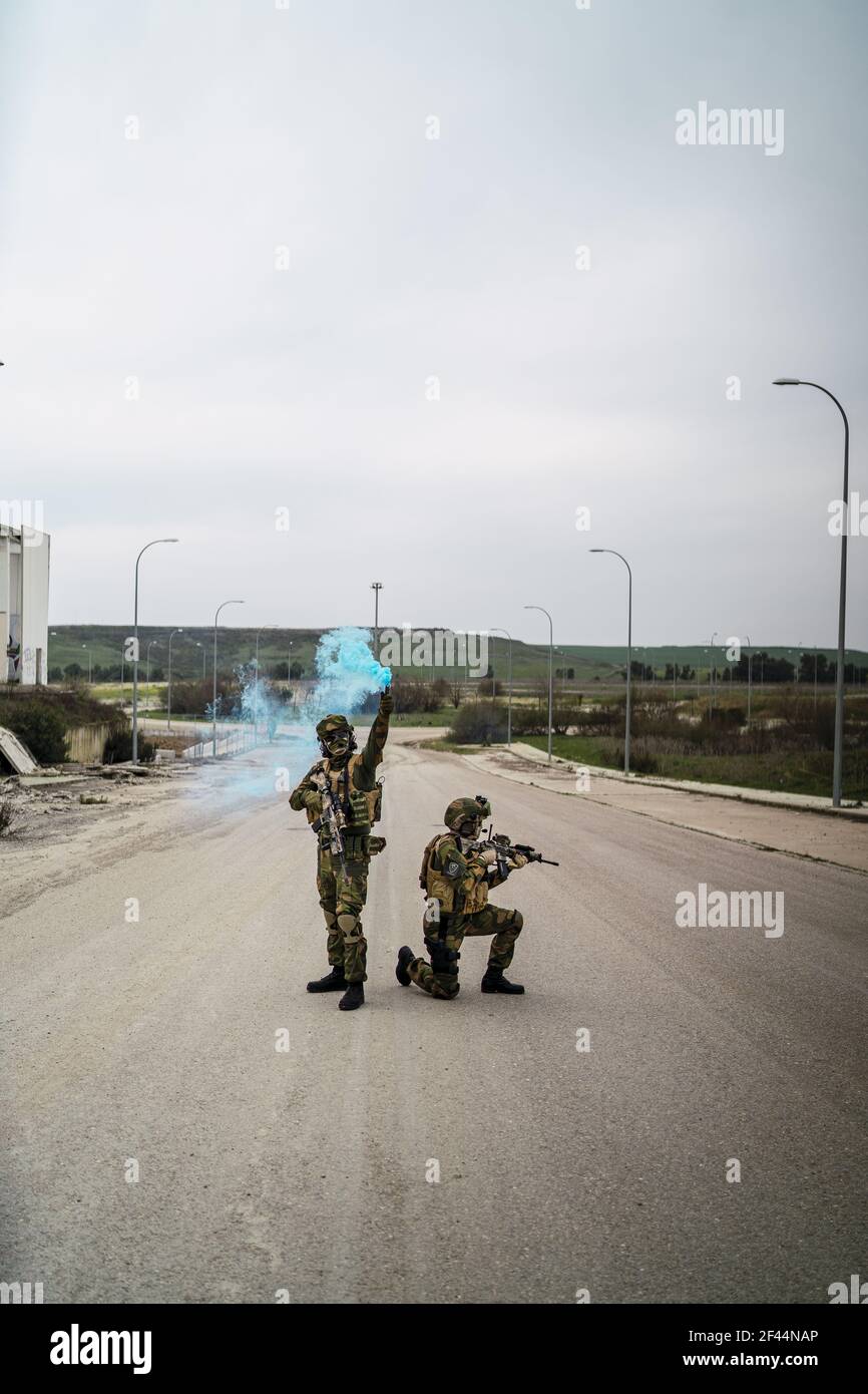 A vertical shot of an armed special force soldier holding a blue smoke ...