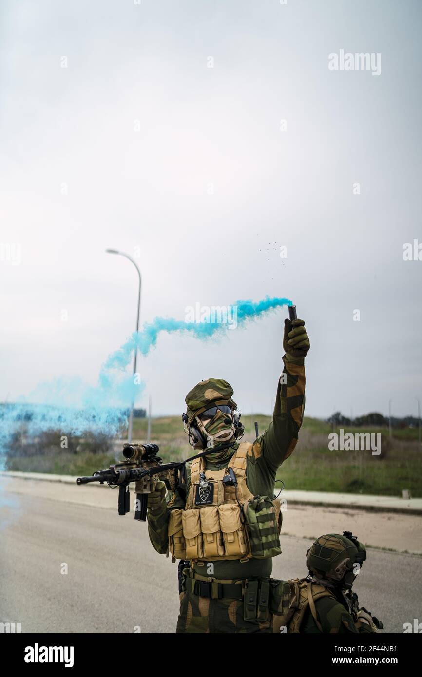 A shallow focus of an armed special force soldier holding a blue smoke ...