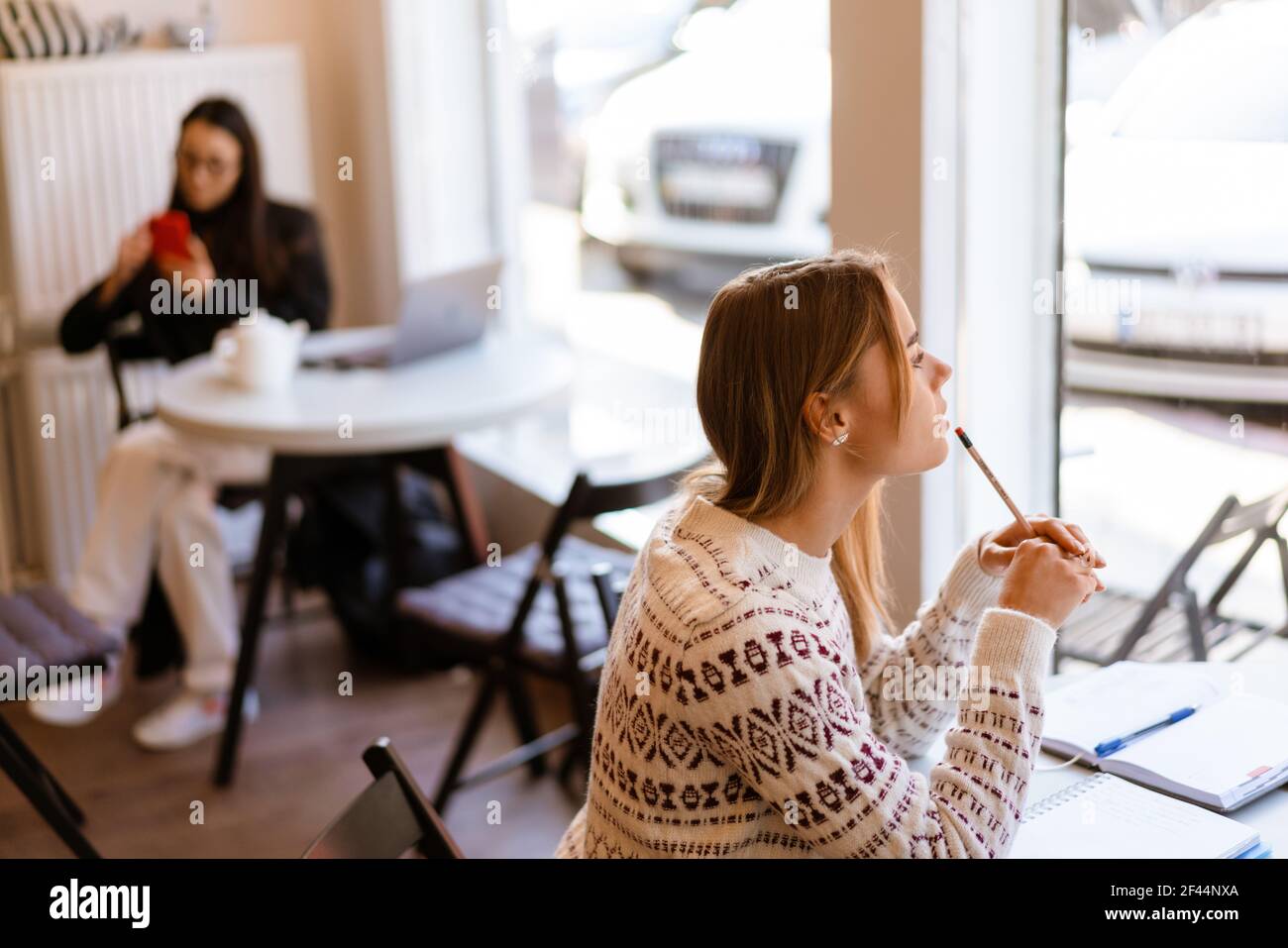 Thinking charming student girl doing homework while sitting in cafe ...
