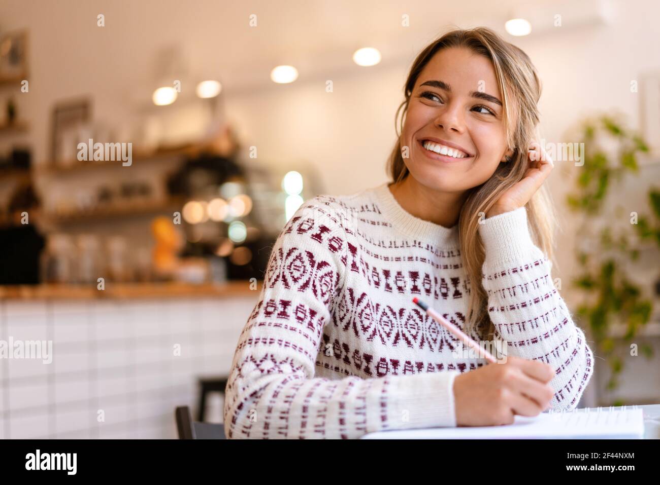 Smiling charming student girl doing homework while sitting in cafe ...