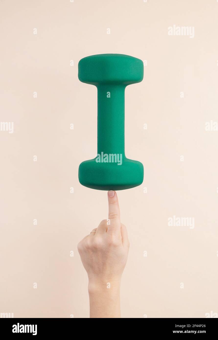 Woman's hand balancing heavy exercise weight on finger for minimal art ...