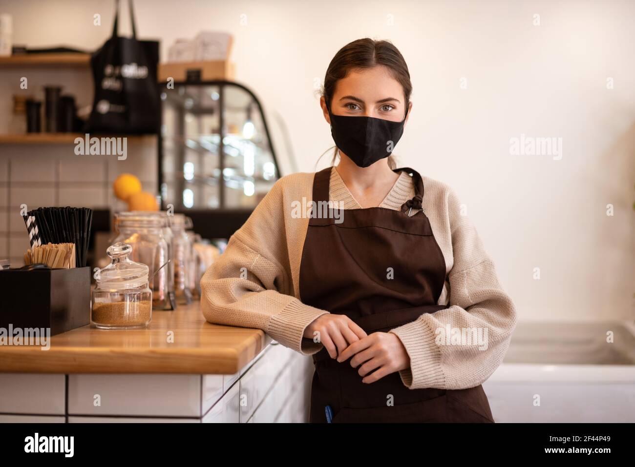 Waitress in a medical protective mask standing and looking at camera in ...