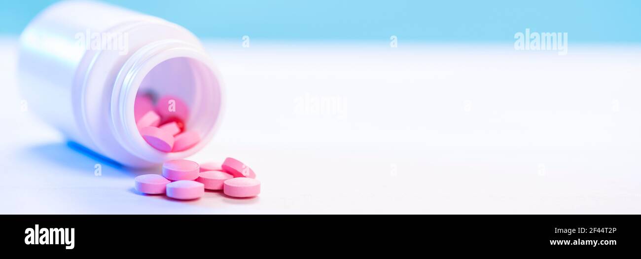 Pink pills are poured from a plastic bottle of medicine onto a white ...