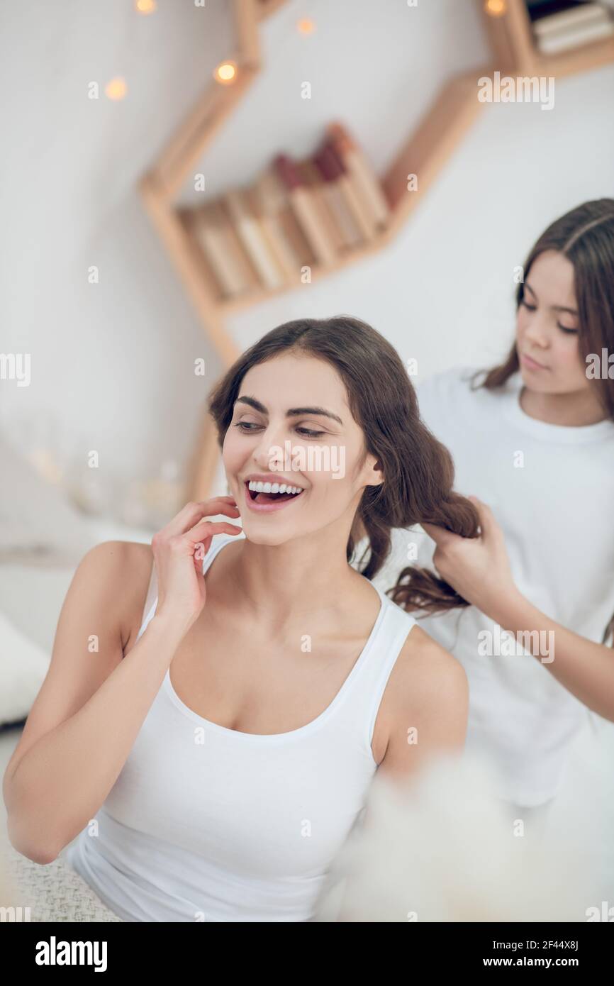 Girl weaving braid to emotional woman in pajamas Stock Photo - Alamy