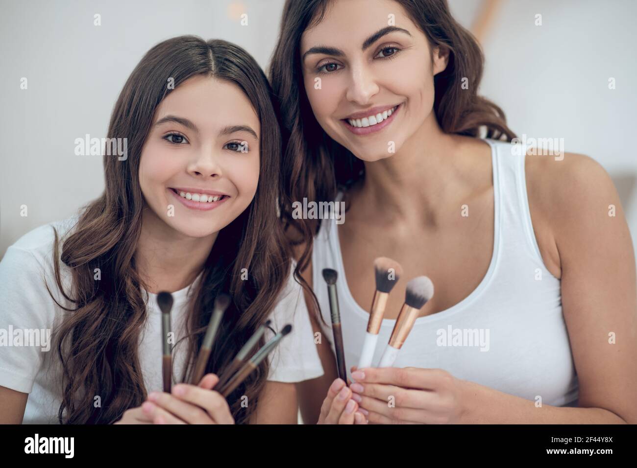 Beautiful mom and daughter with makeup brushes Stock Photo - Alamy