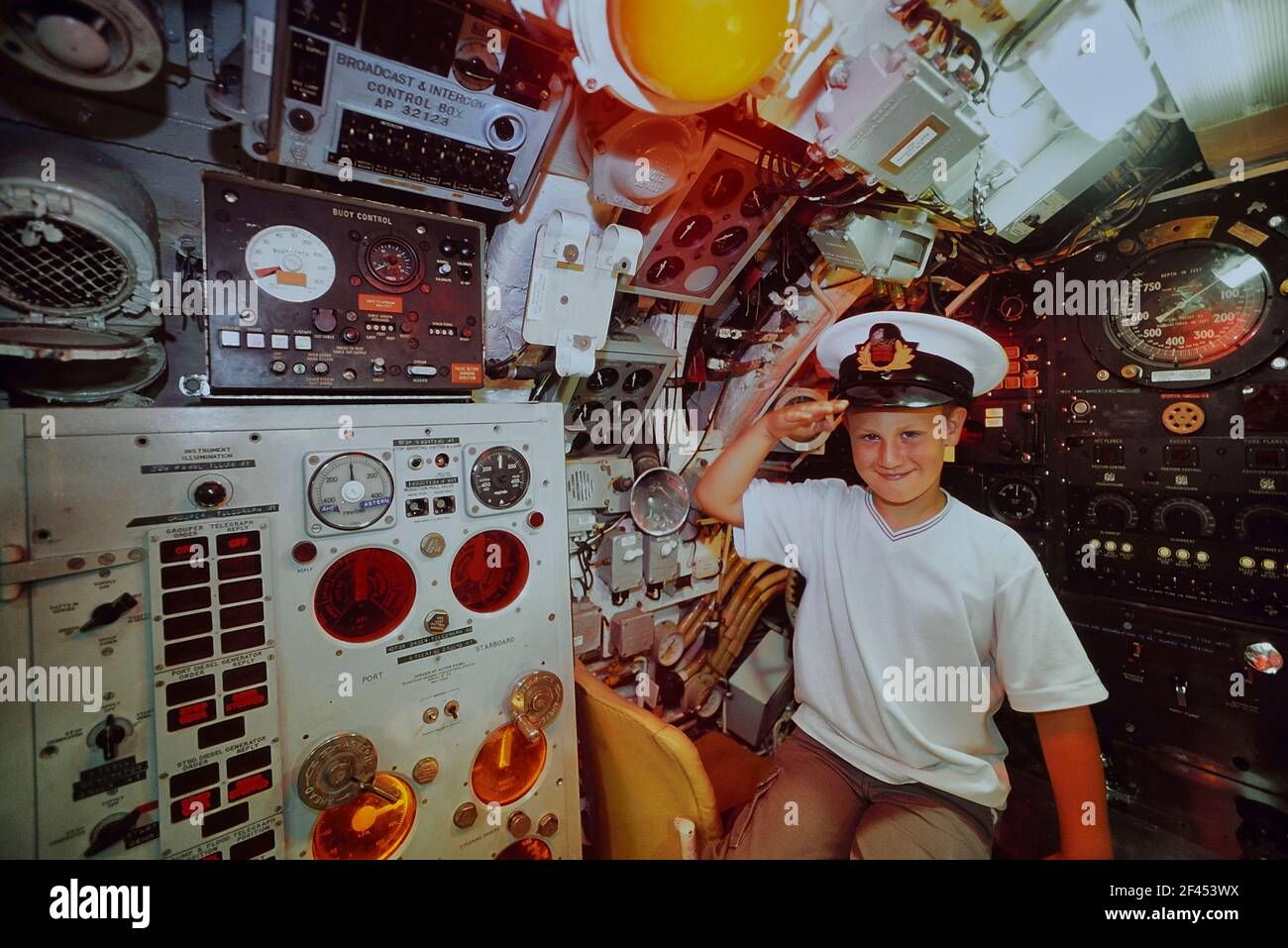 Young boy wearing a Navy officer peak cap saluting from the Helm of the ...