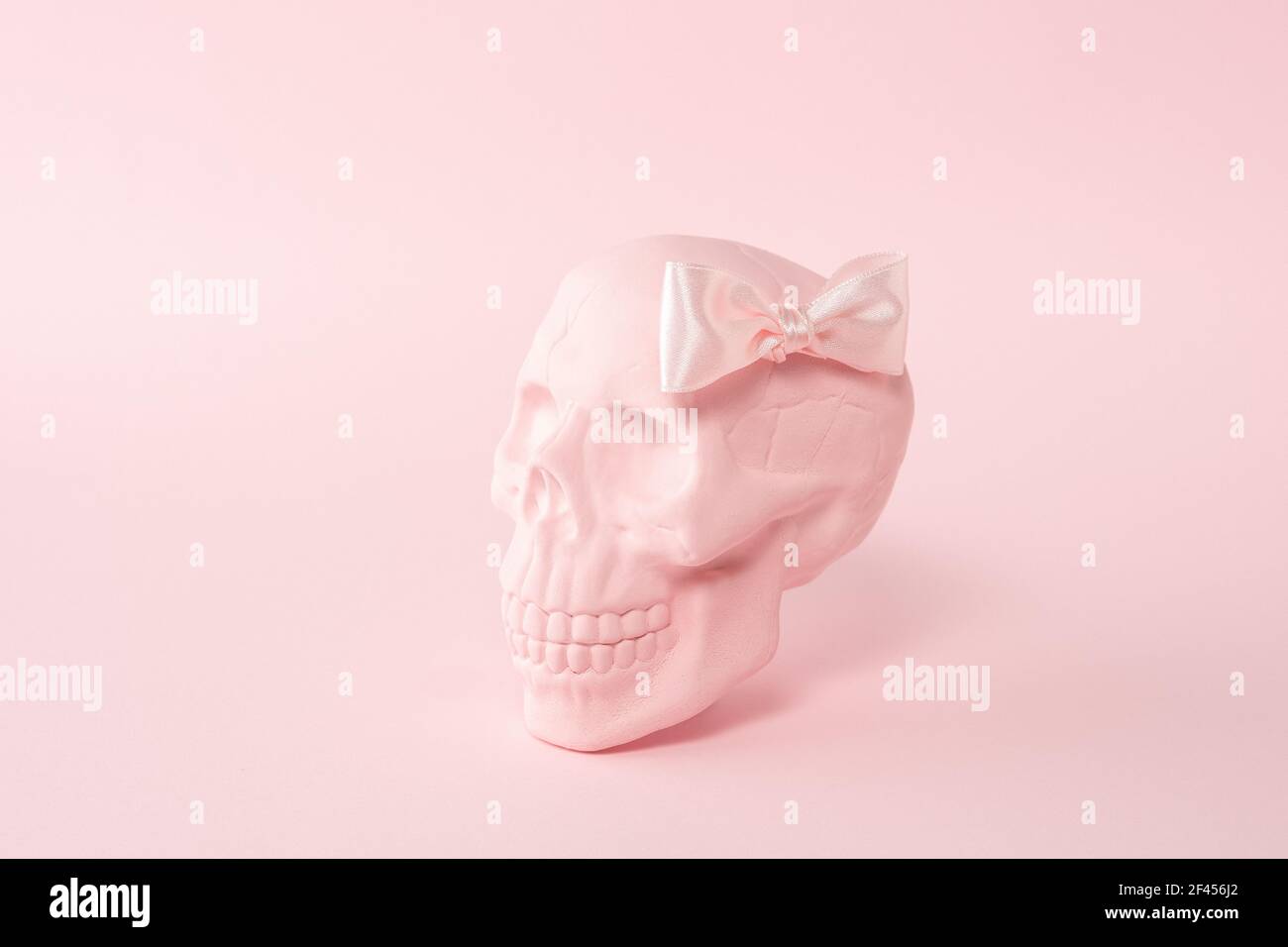 Pink skull with pink bow tie on a pink background. Minimal Halloween ...