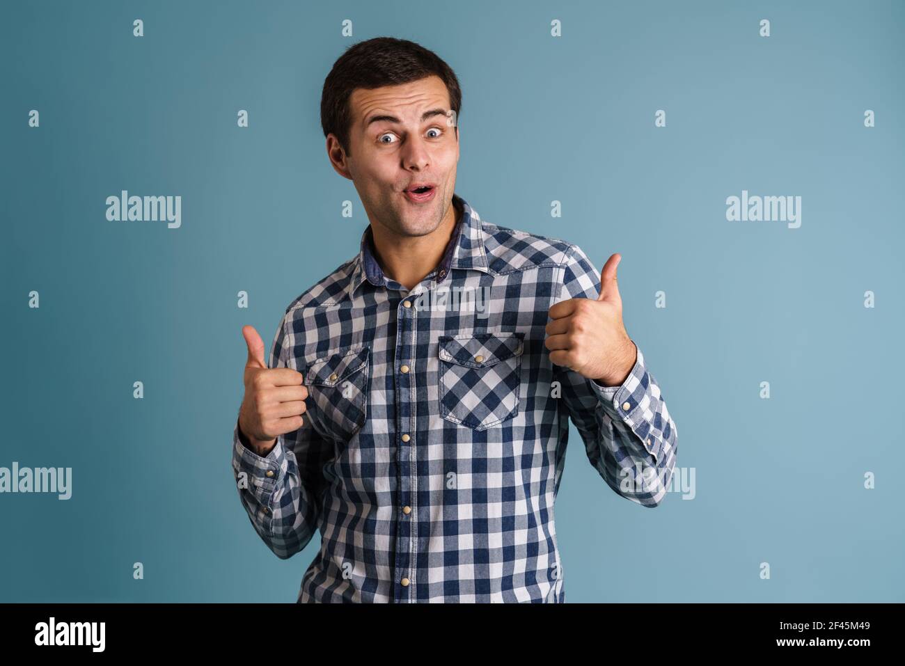 Excited young guy exclaiming while showing thumbs up isolated over blue ...