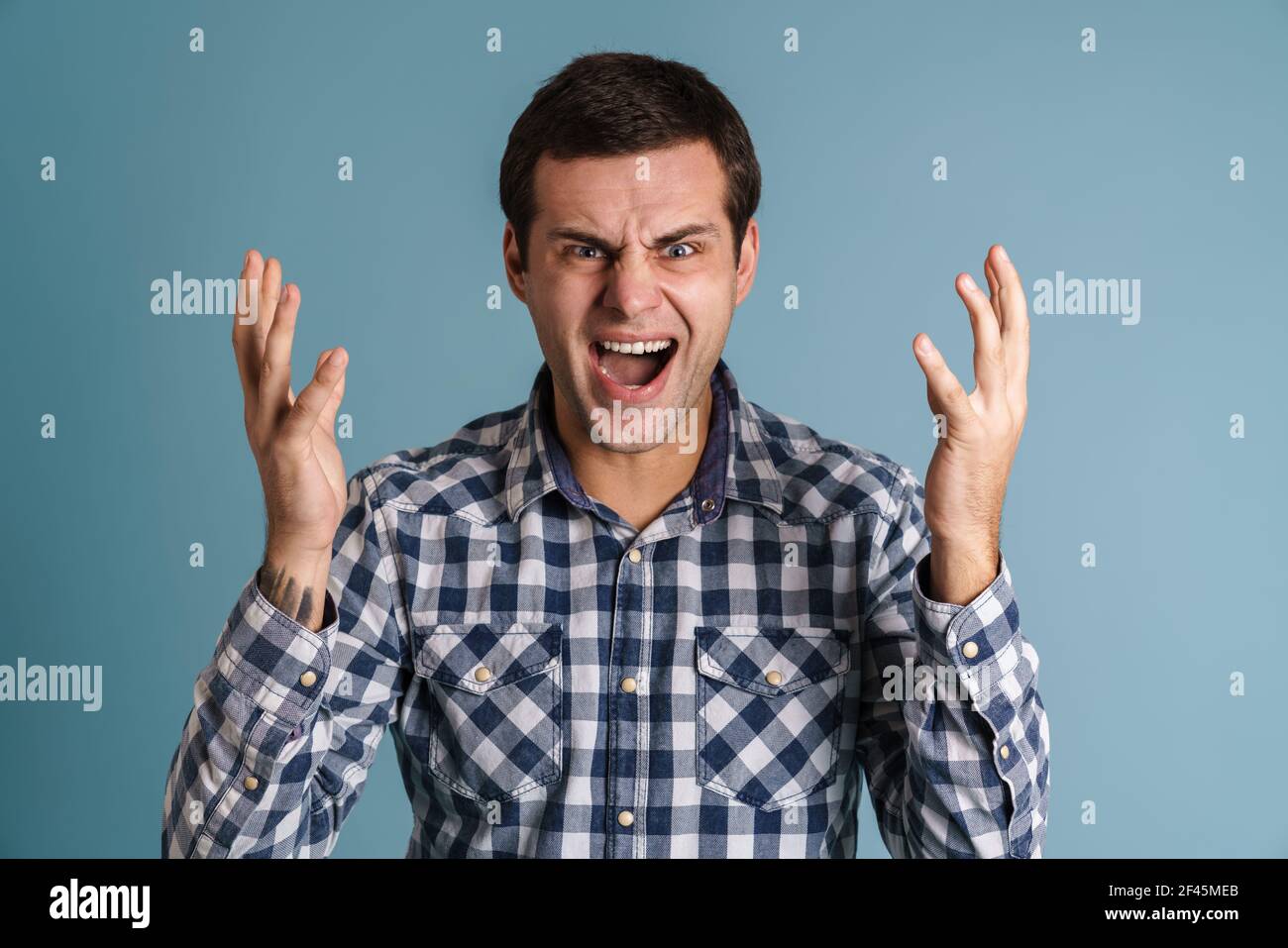 Angry young man screaming isolated over blue background Stock Photo - Alamy