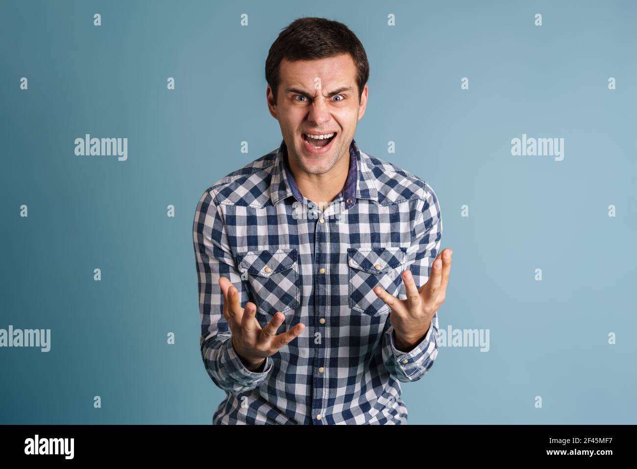 Angry young man screaming isolated over blue background Stock Photo - Alamy