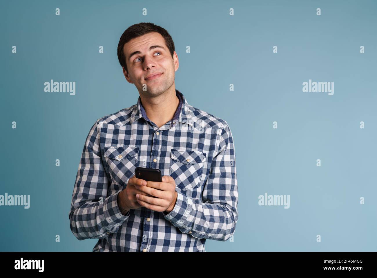 Handsome happy young man using mobile phone isolated over blue ...