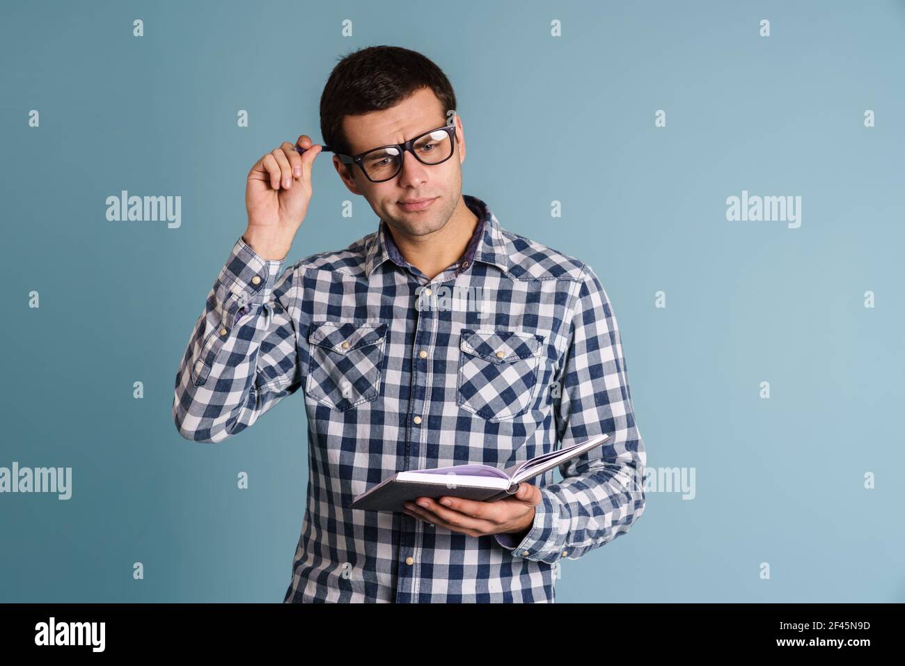 Handsome pensive smart young man writing notes while standing ...