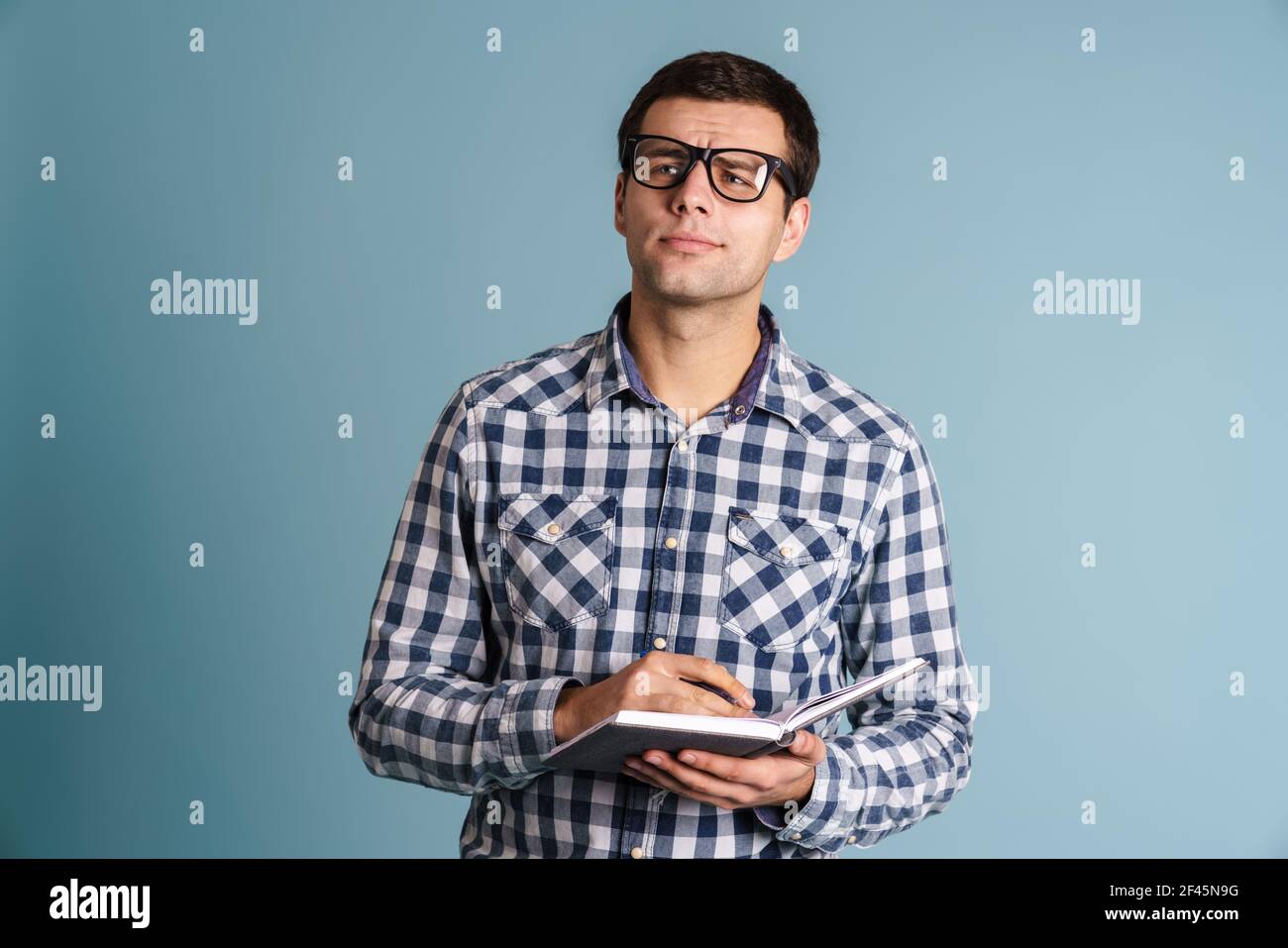Handsome pensive smart young man writing notes while standing ...
